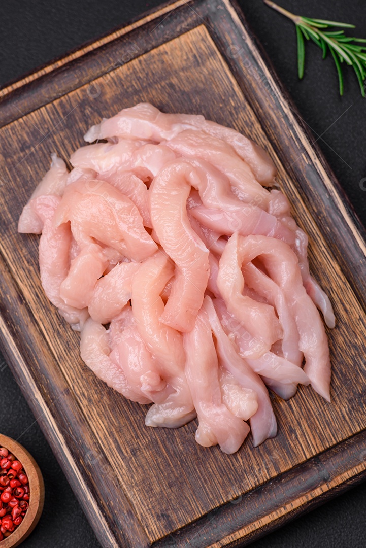 Filé de frango cru cortado em tiras com especiarias e ervas numa tábua ...